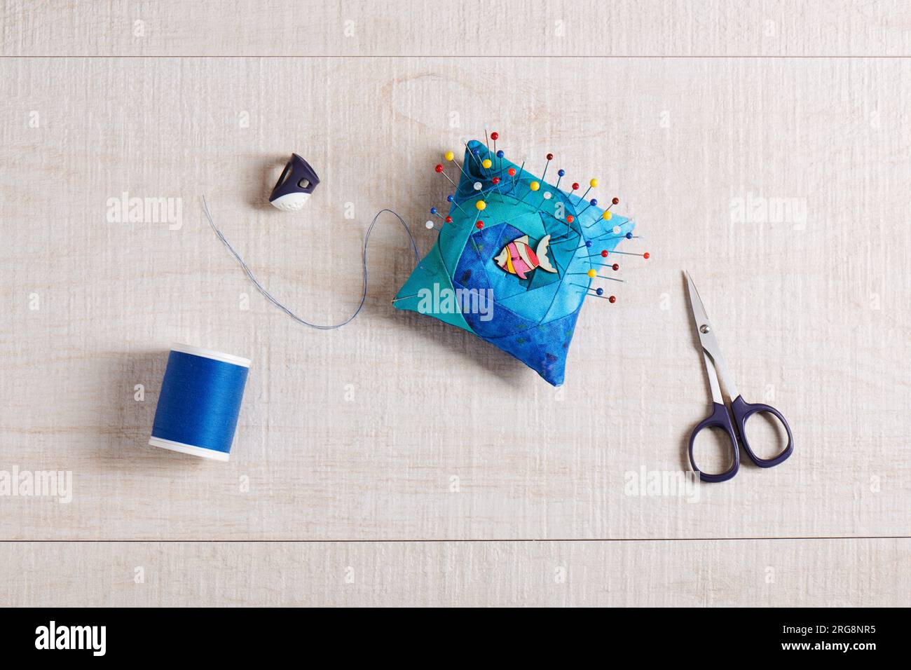 Pin cushion, scissors, spool of thread, thimble on cream-white wooden ...