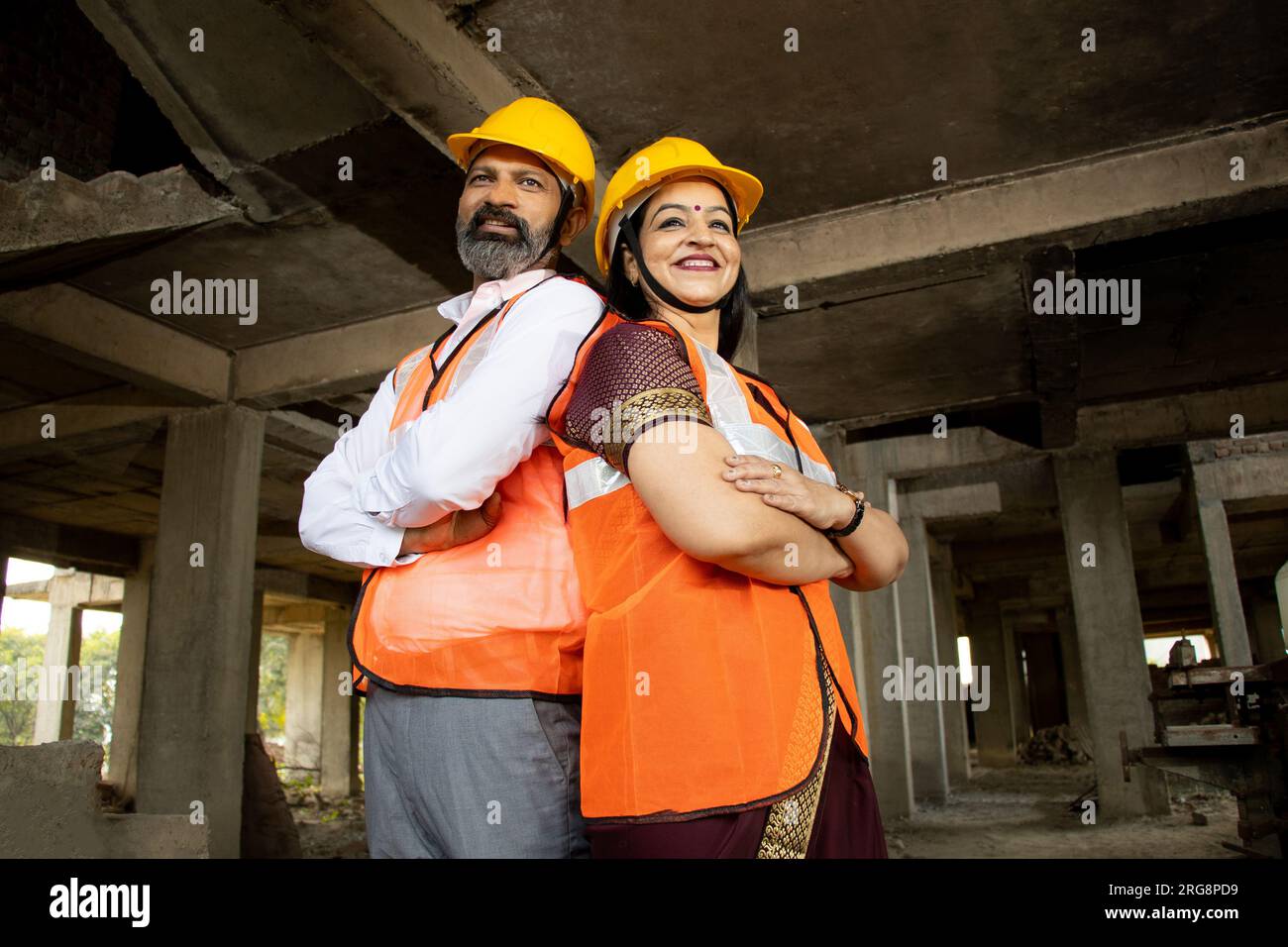 Portrait of two Indian male and female civil engineers or architect wearing helmet standing with ...