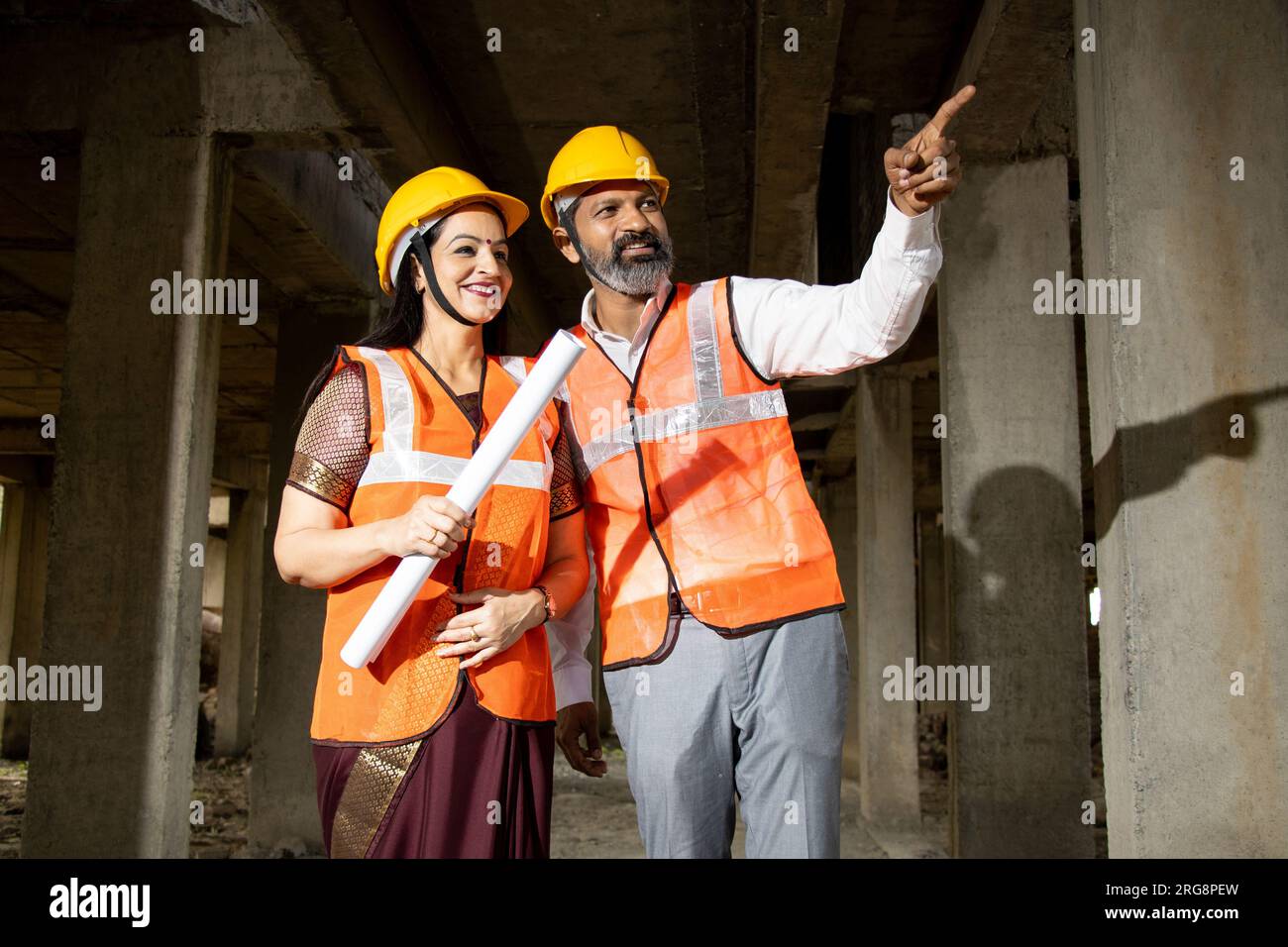Two Indian male and female civil engineers or architect wearing helmet and vest holding ...