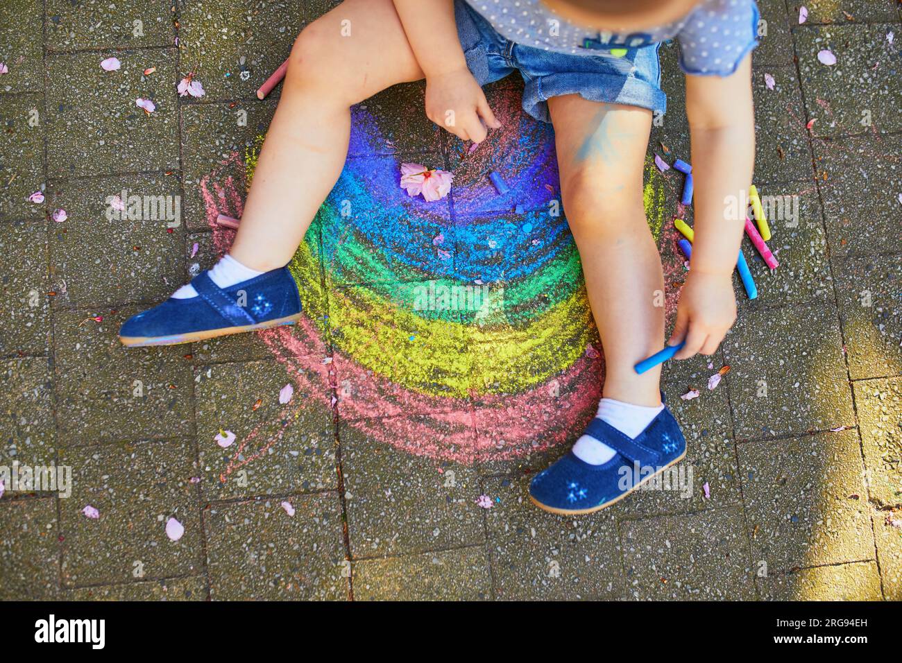 Toddler girl drawing rainbow with colorful chalks on asphalt. Child ...