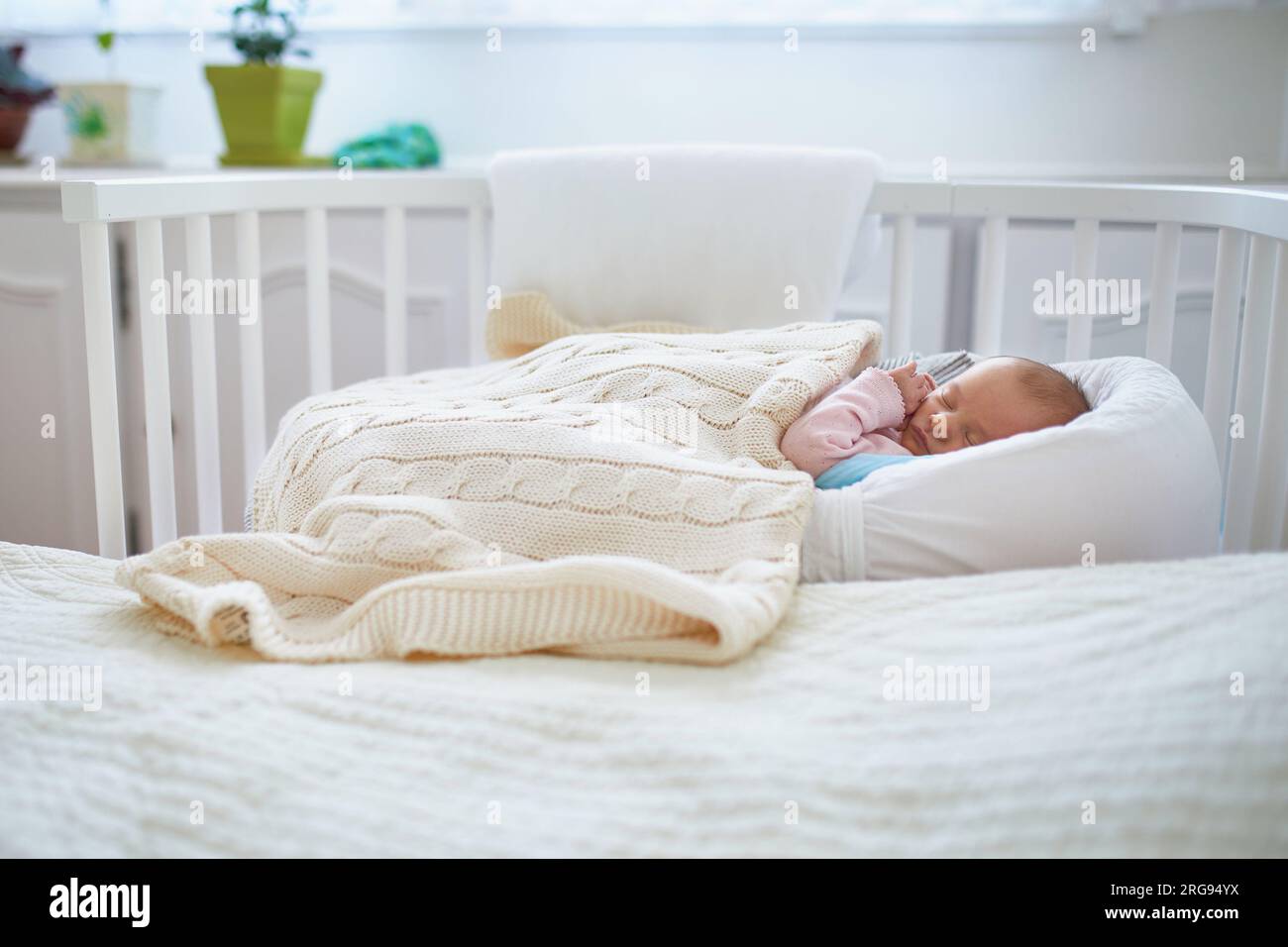 Newborn baby girl having a nap in co-sleeper crib attached to parents ...