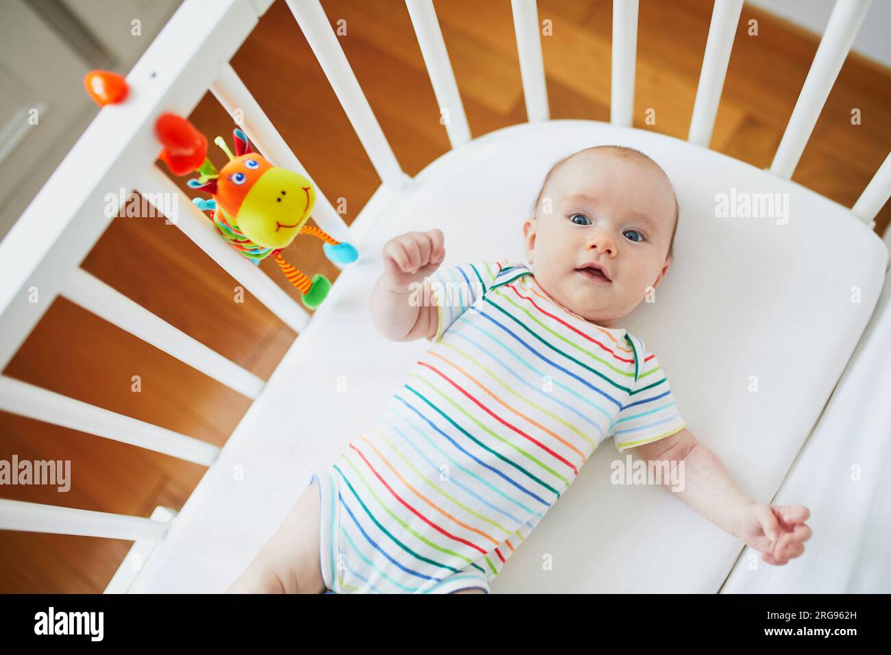Adorable baby girl in co-sleeper crib attached to parents' bed. Little ...