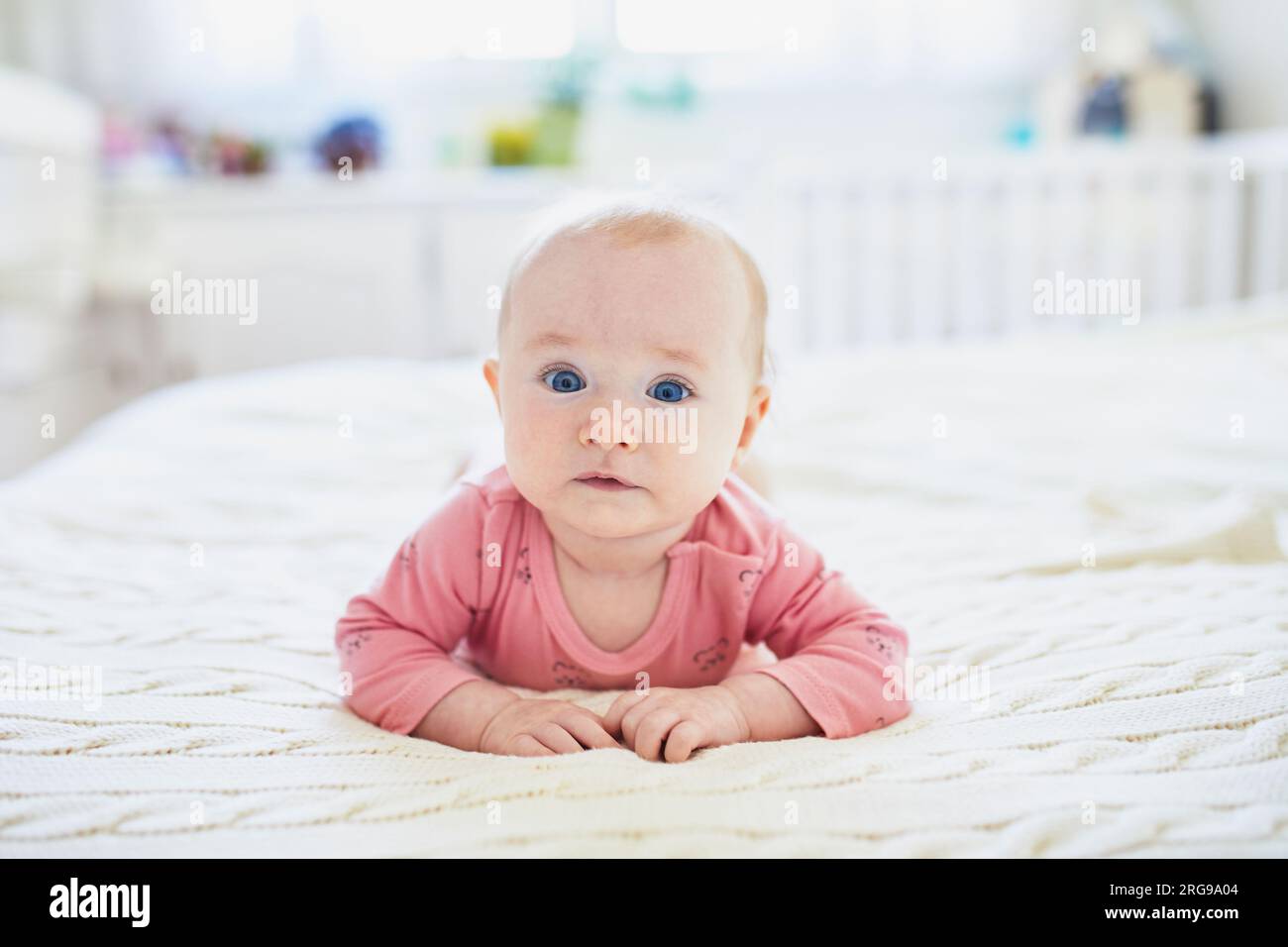 Adorable baby girl lying on bed on her tummy. Happy healthy little ...