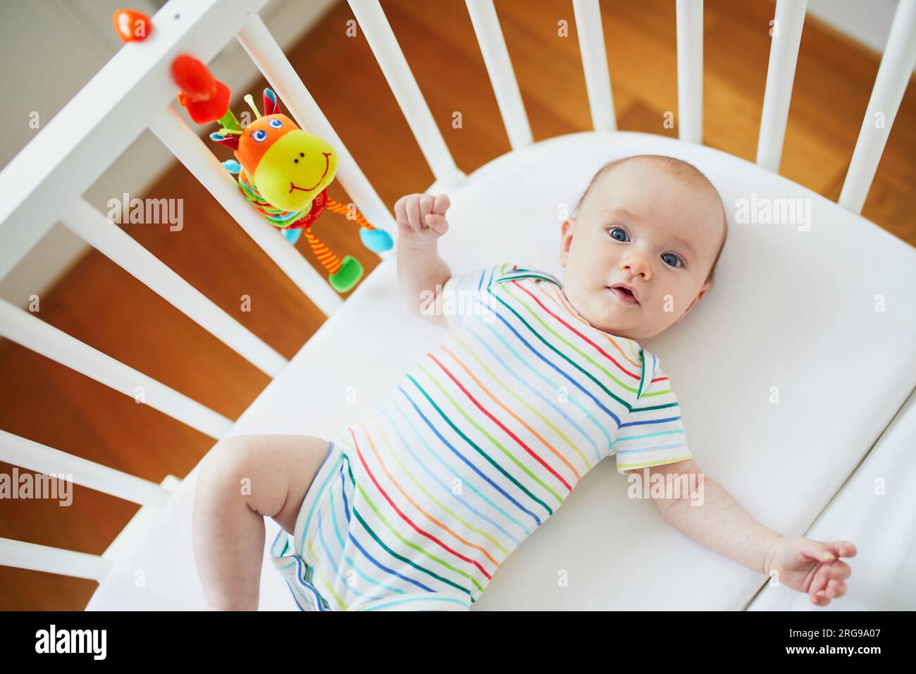 Adorable baby girl in co-sleeper crib attached to parents' bed. Little ...