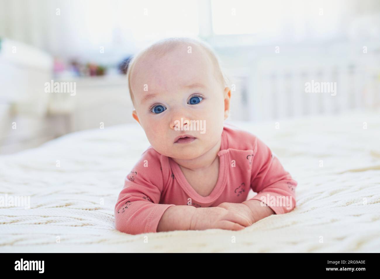 Adorable baby girl lying on bed on her tummy. Happy healthy little ...