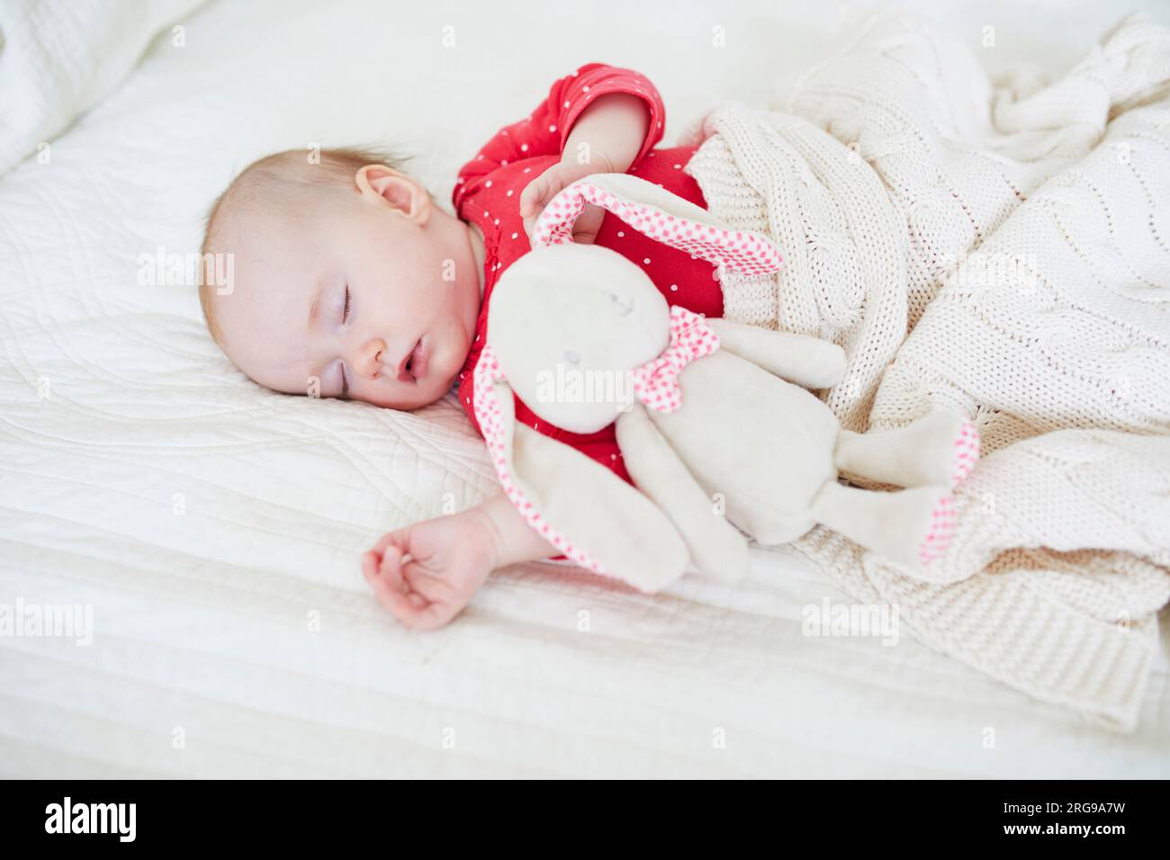 Baby girl sleeping under knitted blanket with her favorite toy. Little ...