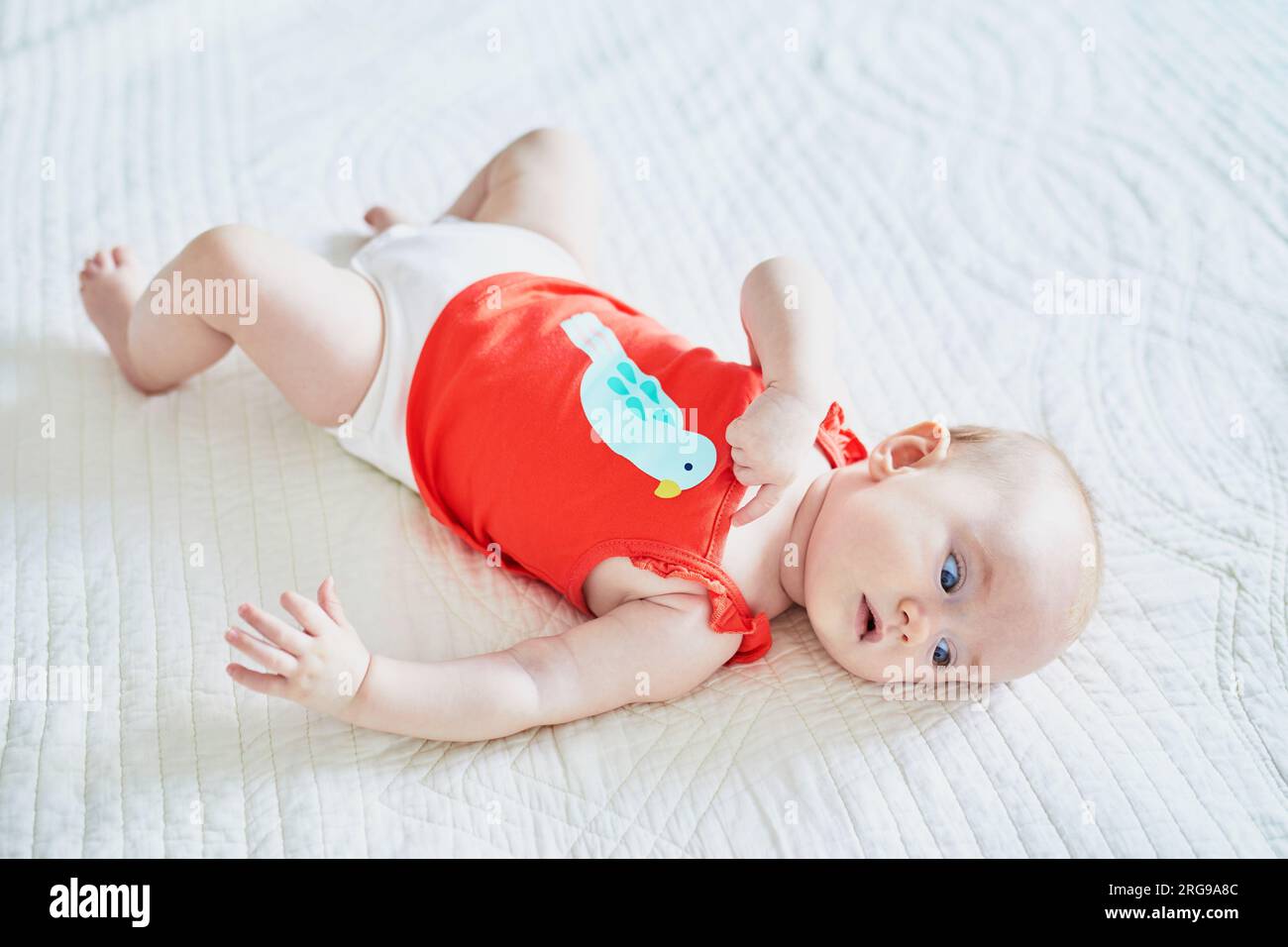 Cute baby girl lying on her back on bed. Happy healthy kid in nursery ...
