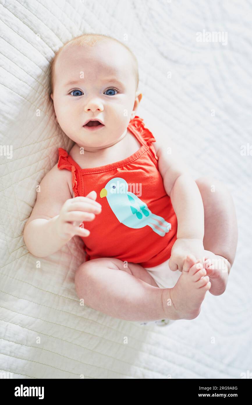 Cute baby girl lying on her back and touching her feet. Happy healthy ...
