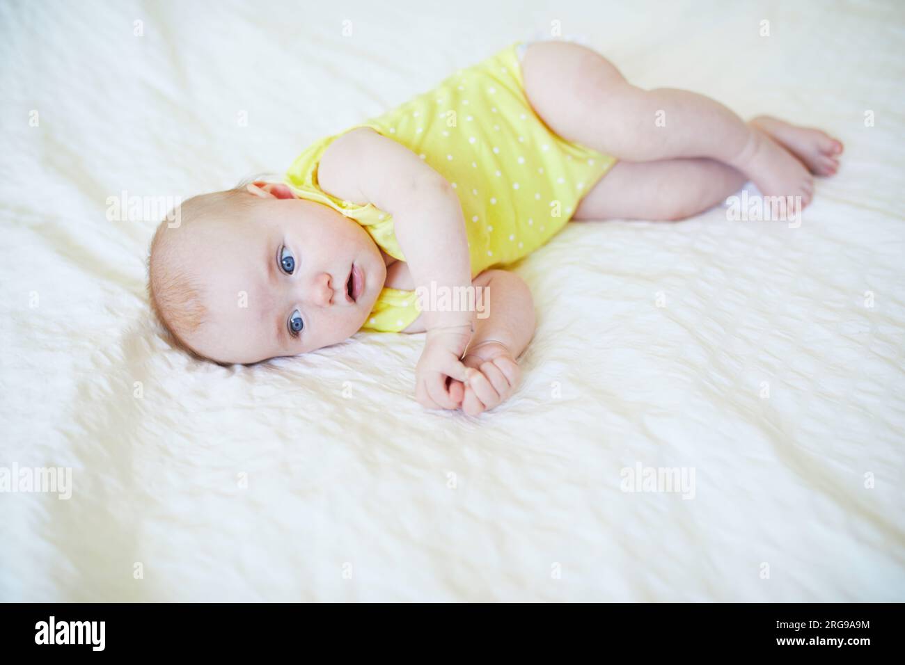 Cute baby girl lying on her back on bed. Happy healthy kid in nursery ...