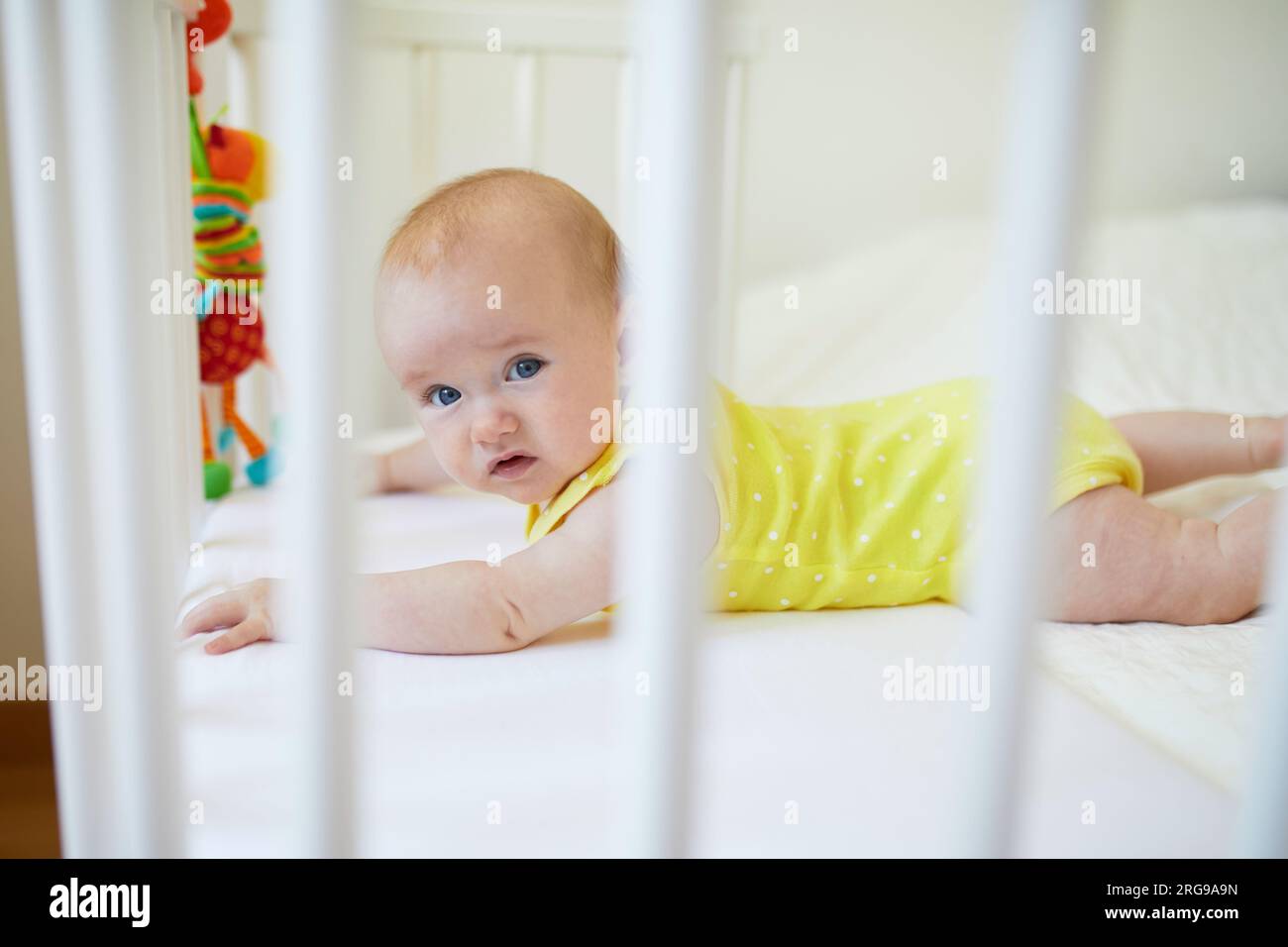 Adorable baby girl lying in co-sleeper crib attached to parents' bed ...