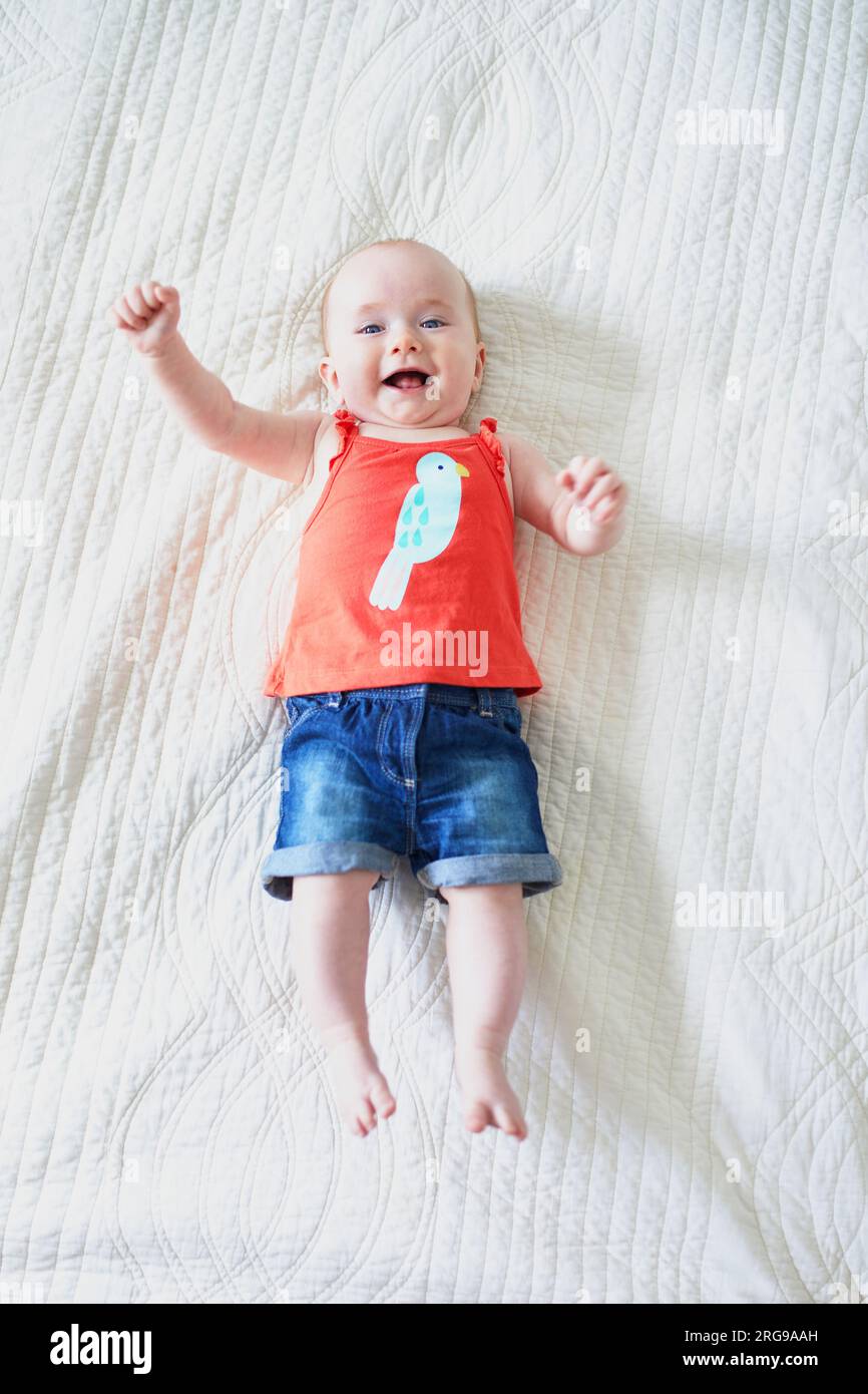 Six months old baby girl lying on her back and laughing. Happy kid wearing jeans shorts and t ...