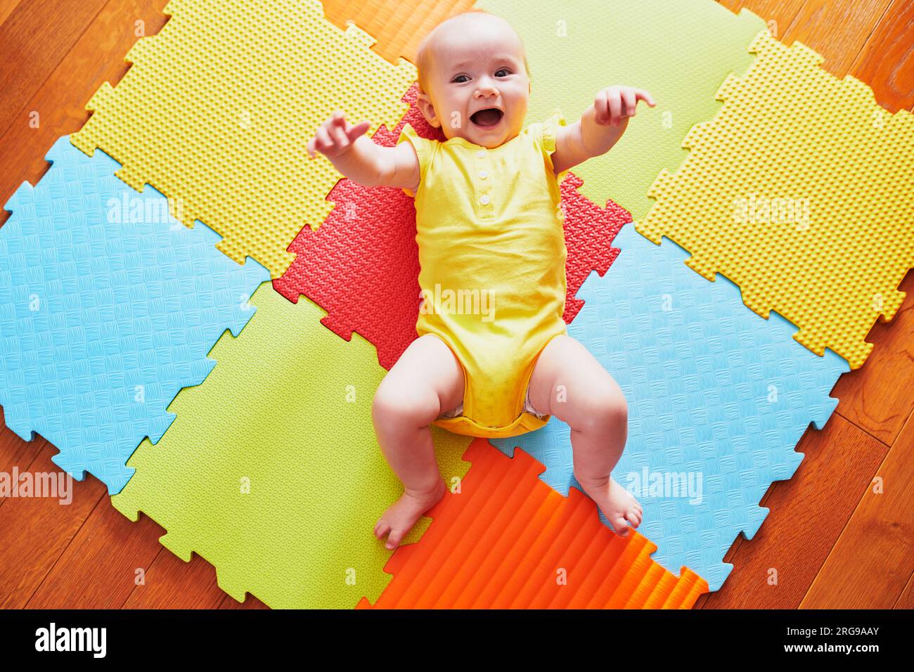 Happy smiling baby girl lying on colorful play mat on the floor, view ...