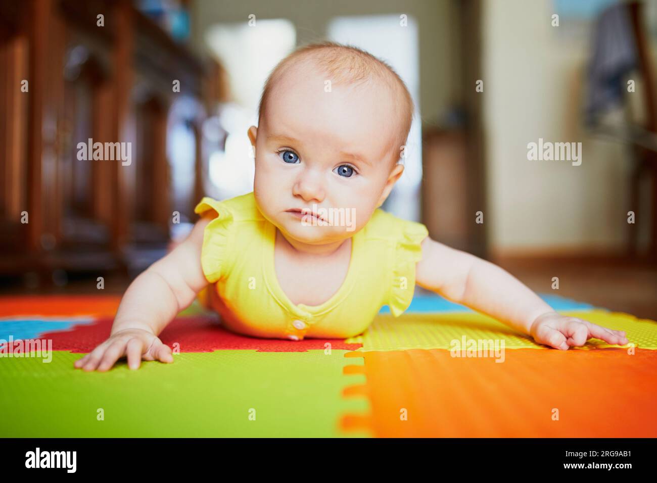 Adorable baby girl doing tummy time on colorful play mat Stock Photo ...