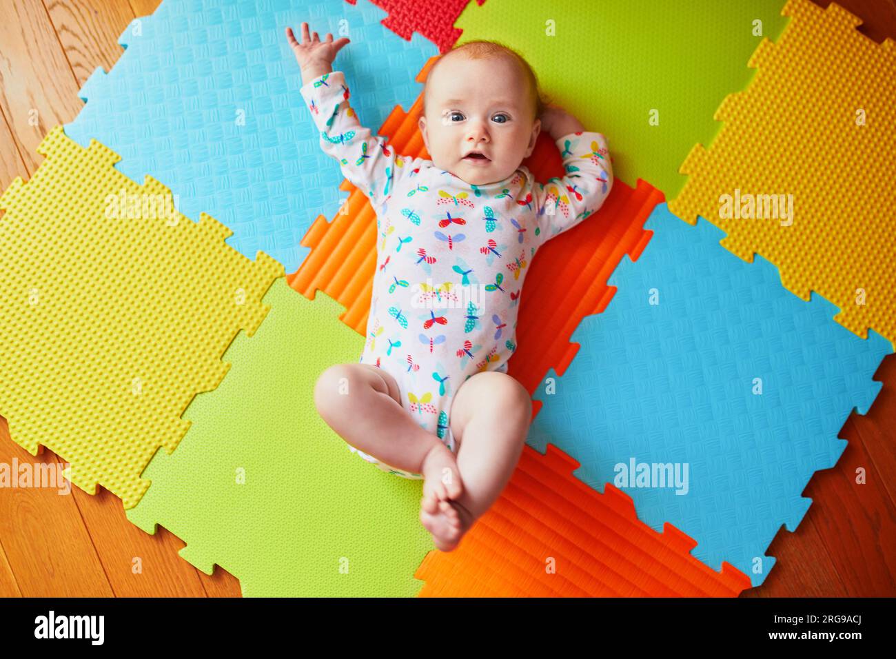 4 months old baby girl lying on colorful play mat on the floor ...