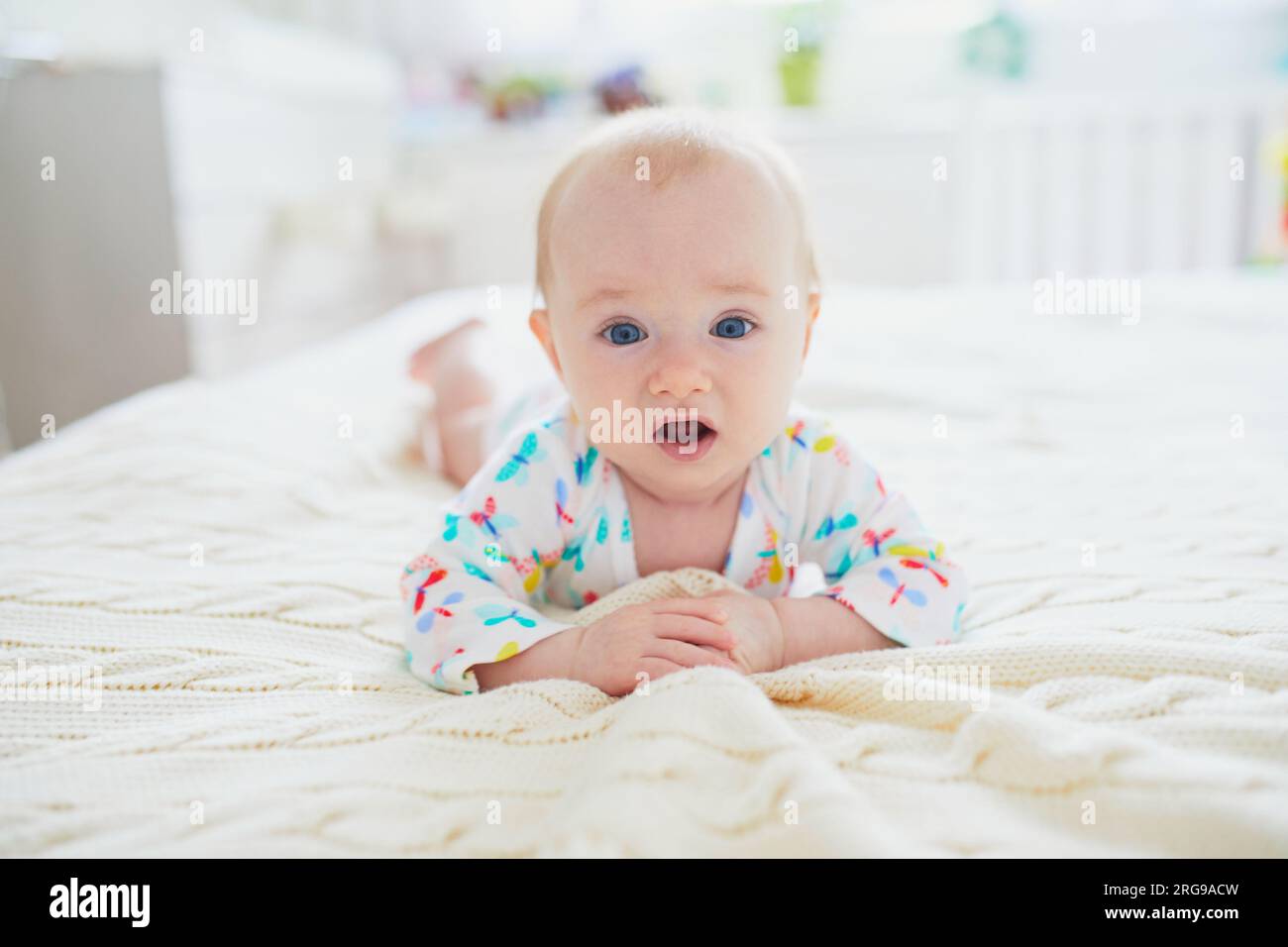 Adorable baby girl lying on bed on her tummy. Happy healthy little ...