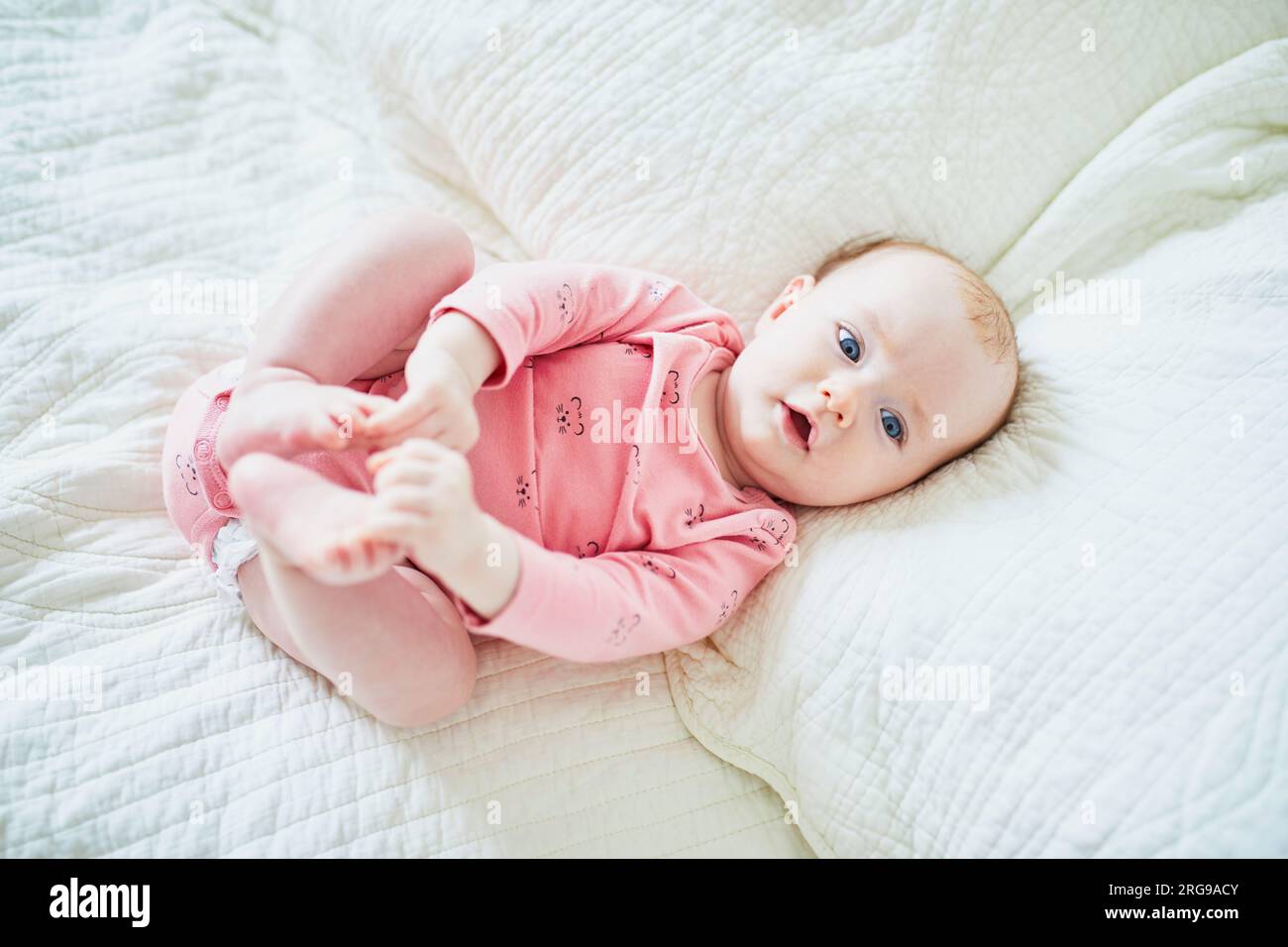 Baby girl lying on bed on her back and touching her toes. Happy healthy ...