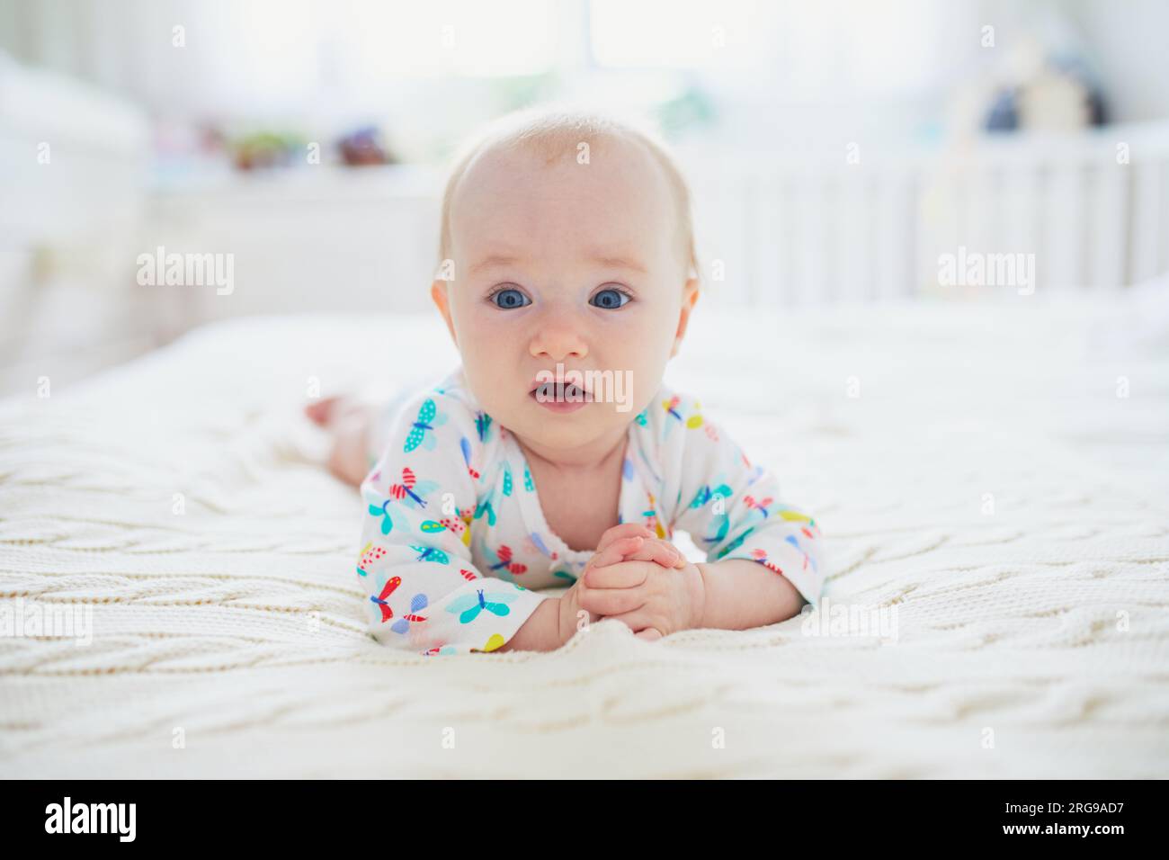 Adorable baby girl lying on bed on her tummy. Happy healthy little ...