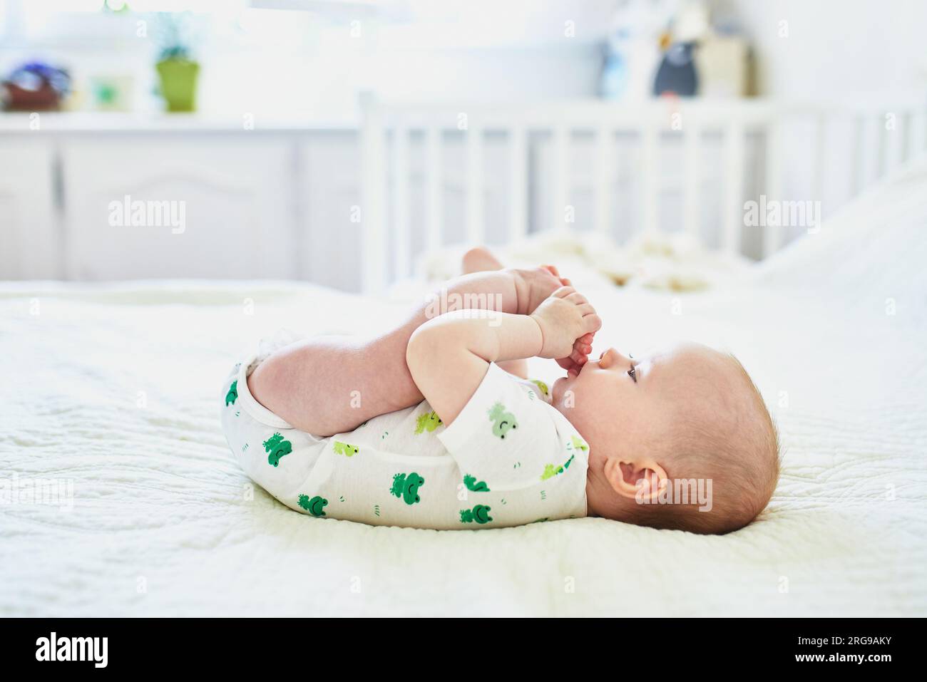 Baby girl putting her feet into mouth and suckling toes. Little child ...