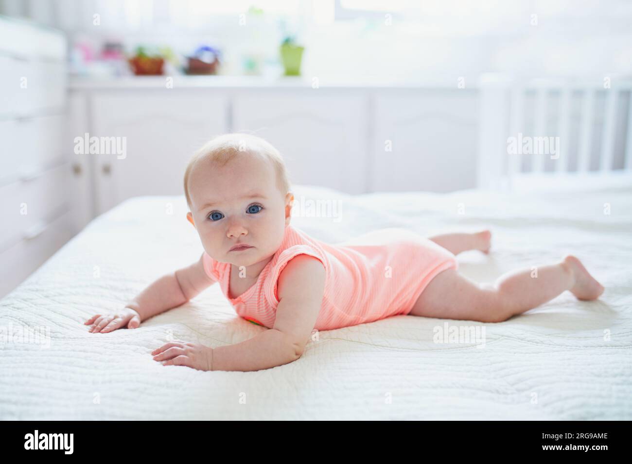 Cute baby girl lying on her tummy. Happy healthy kid at home in nursery ...