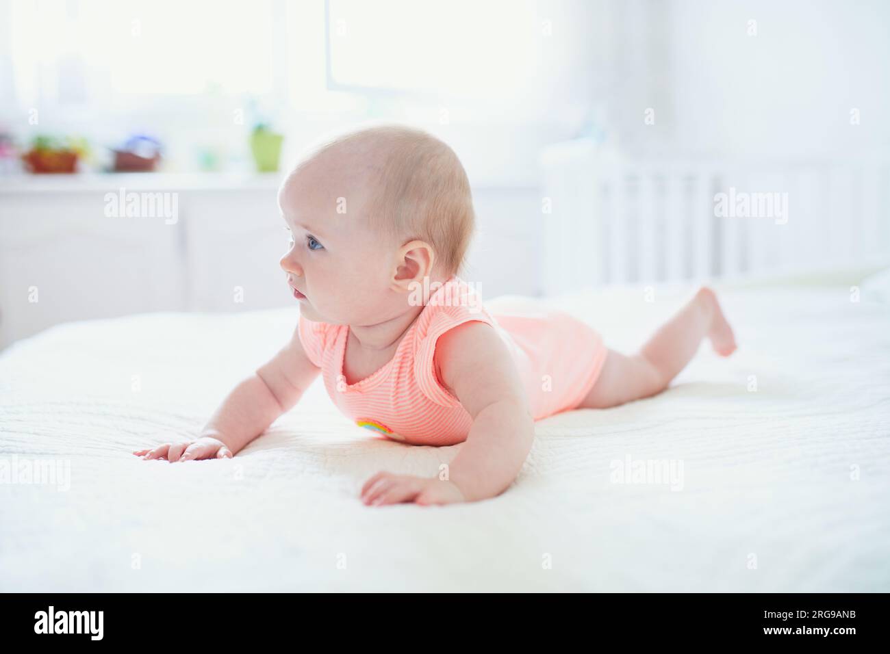 Cute baby girl lying on her tummy. Happy healthy kid at home in nursery ...