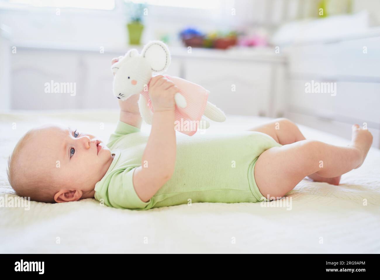 Cute baby girl lying on her back on bed with soft toy. Happy healthy ...