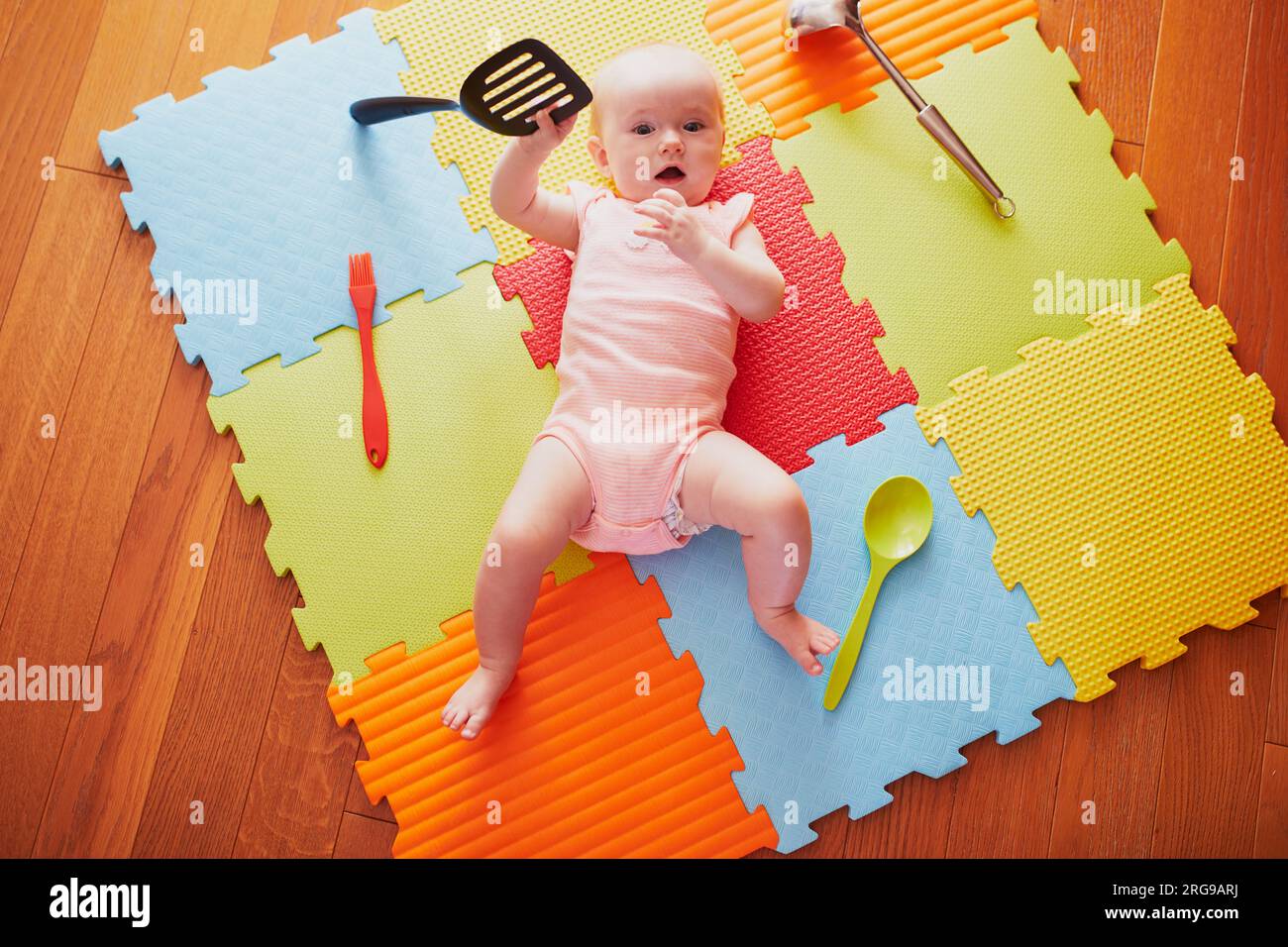 Baby girl with kitchen utensils. Little child lying playmat and playing ...