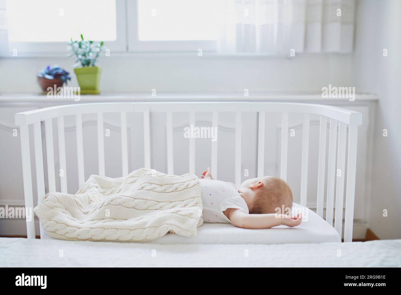 Adorable baby girl sleeping in co-sleeper crib attached to parents' bed ...