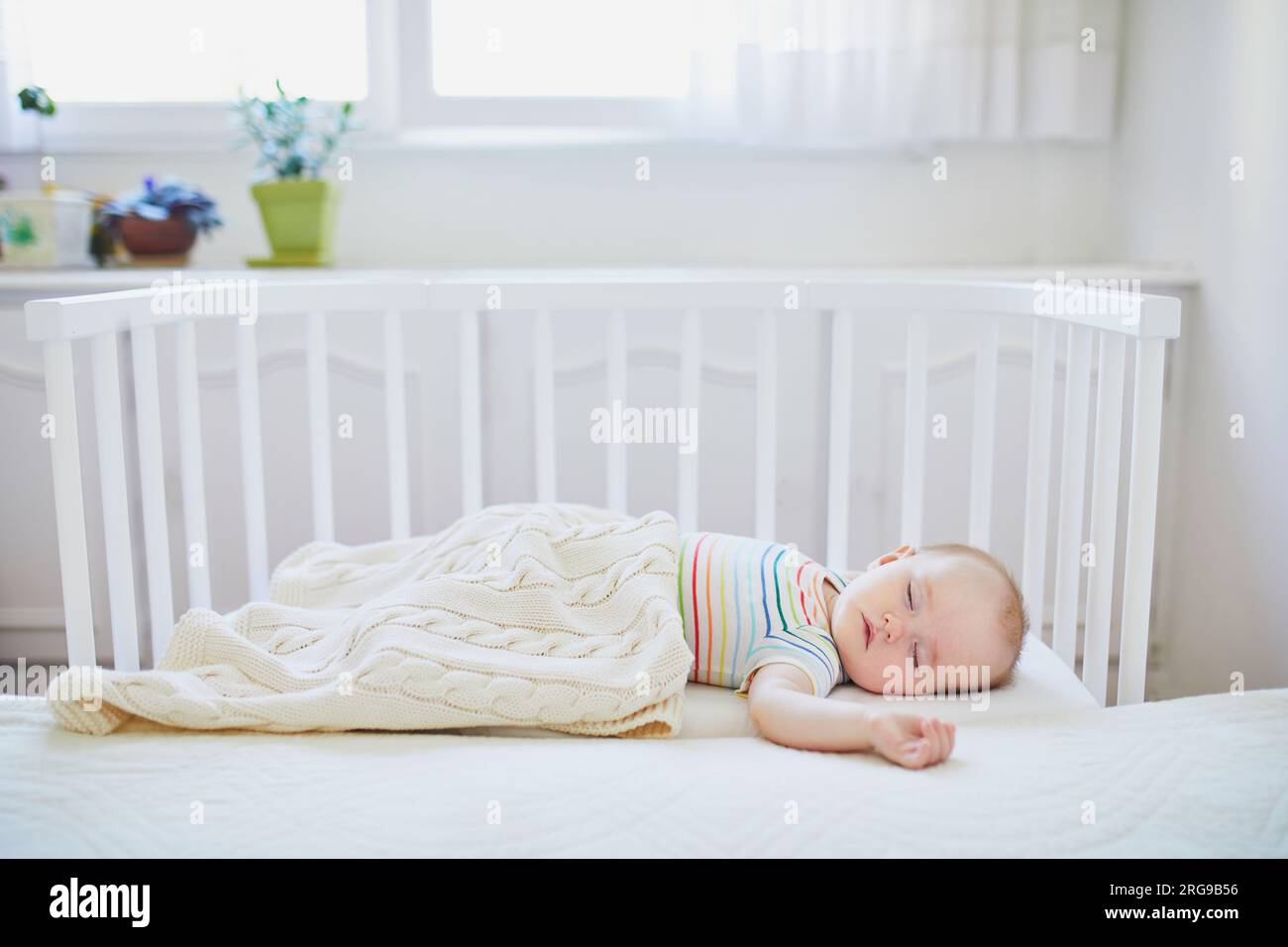 Adorable baby girl sleeping in co-sleeper crib attached to parents' bed ...