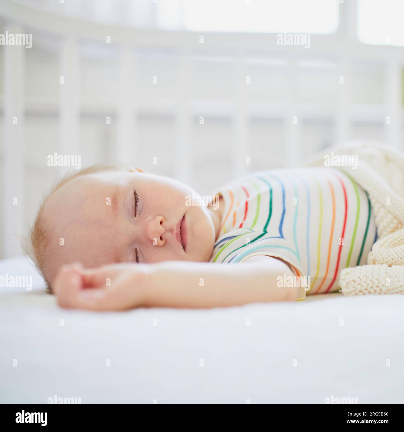 Adorable baby girl sleeping in co-sleeper crib attached to parents' bed ...