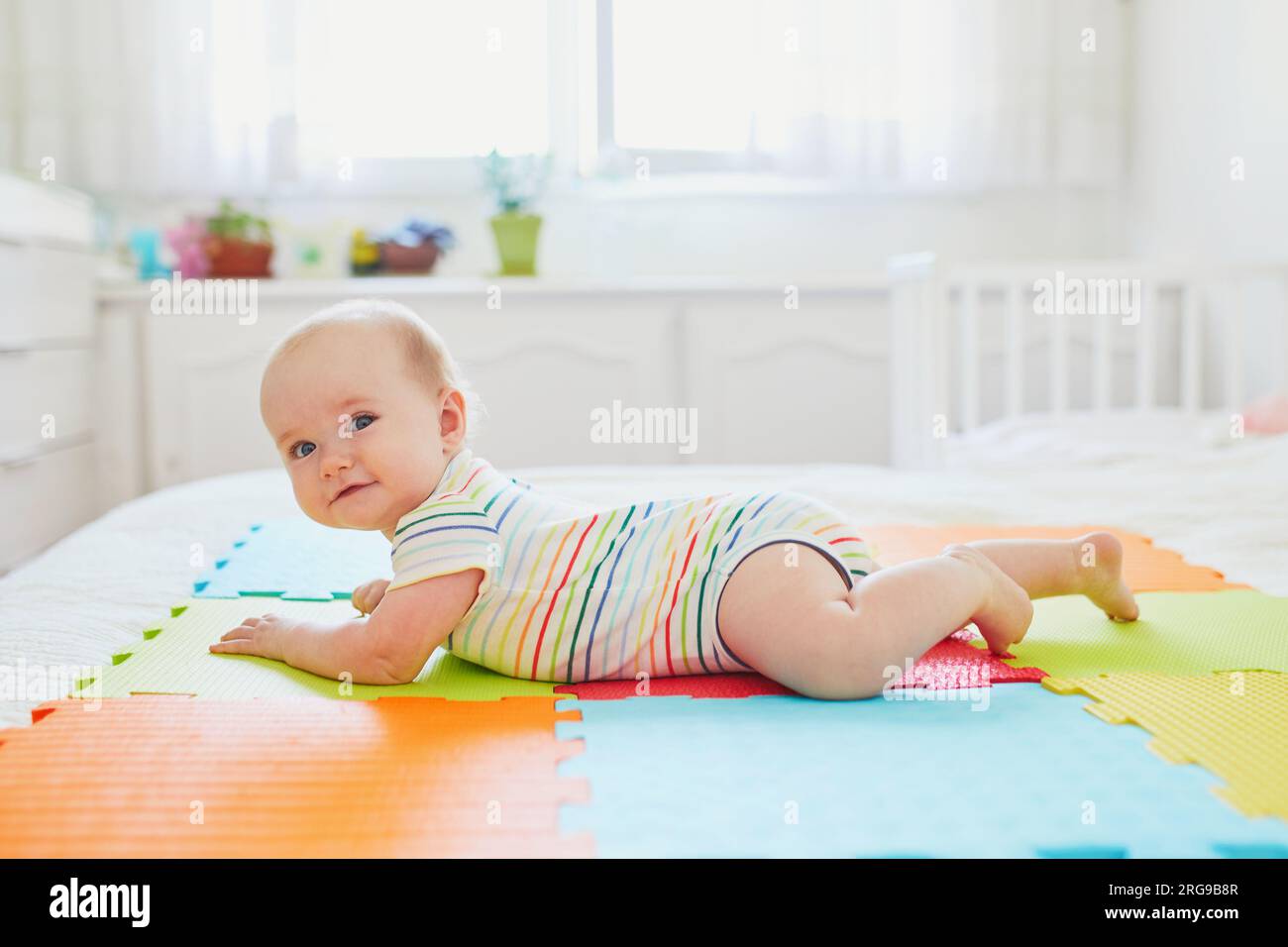 Happy smiling baby girl lying on colorful play mat on the floor Stock ...