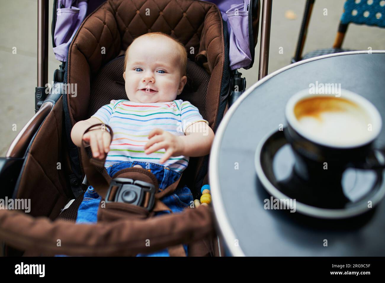 Smiling baby girl in stroller near the table of Parisian outdoor cafe ...