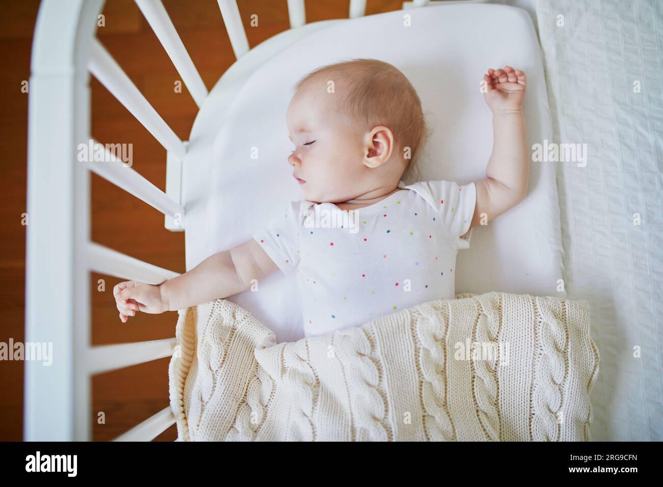 Adorable baby girl sleeping in co-sleeper crib attached to parents' bed ...