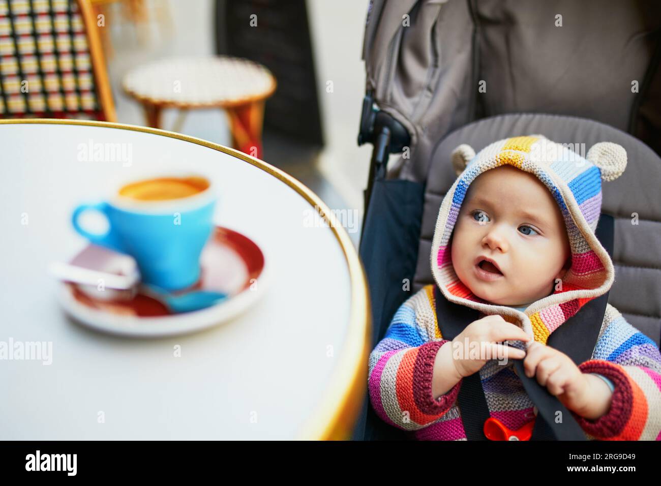 Baby girl in stroller near the table of Parisian outdoor cafe with cup ...