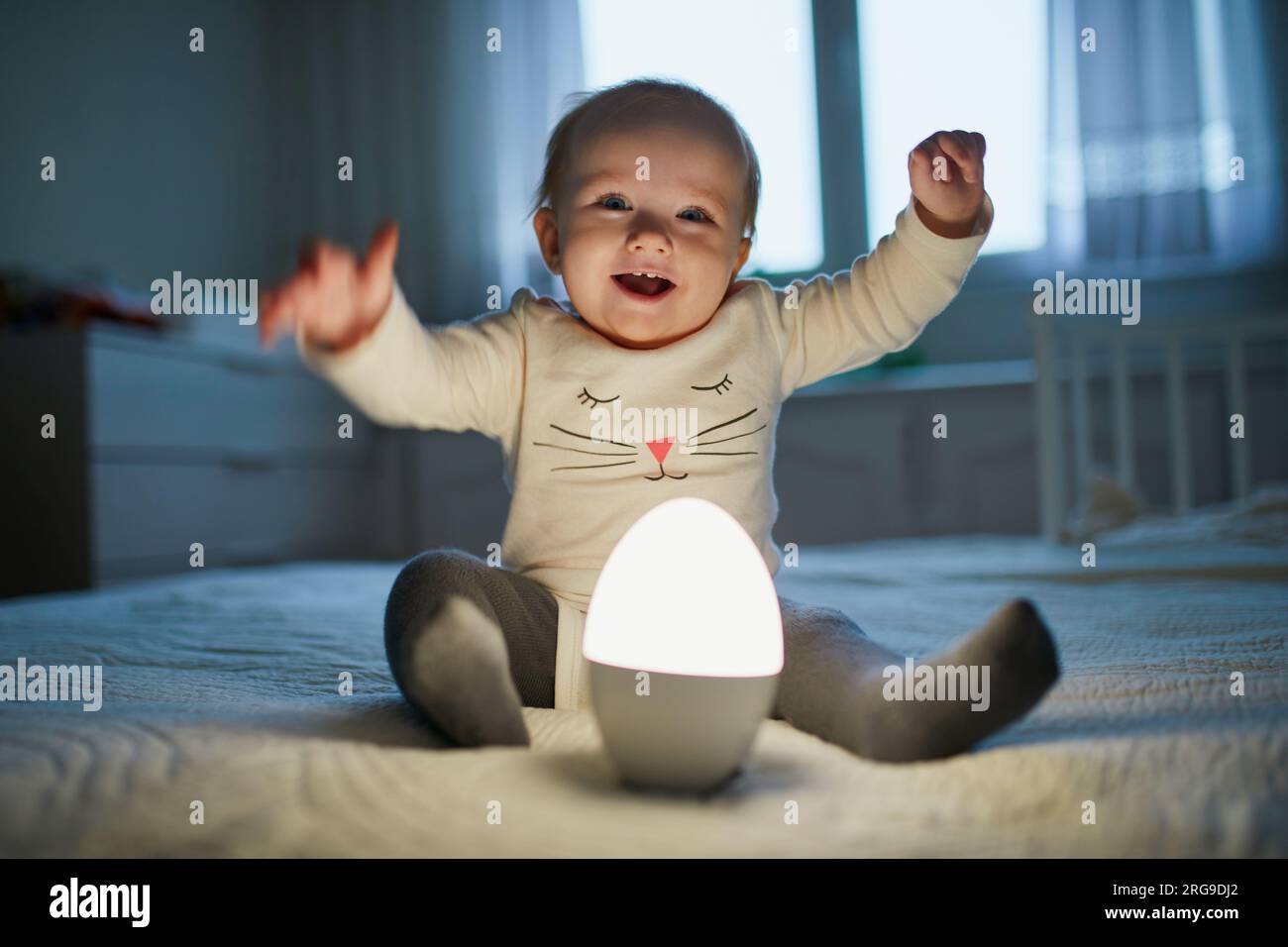 Adorable baby girl playing with bedside lamp in nursery. Happy kid ...