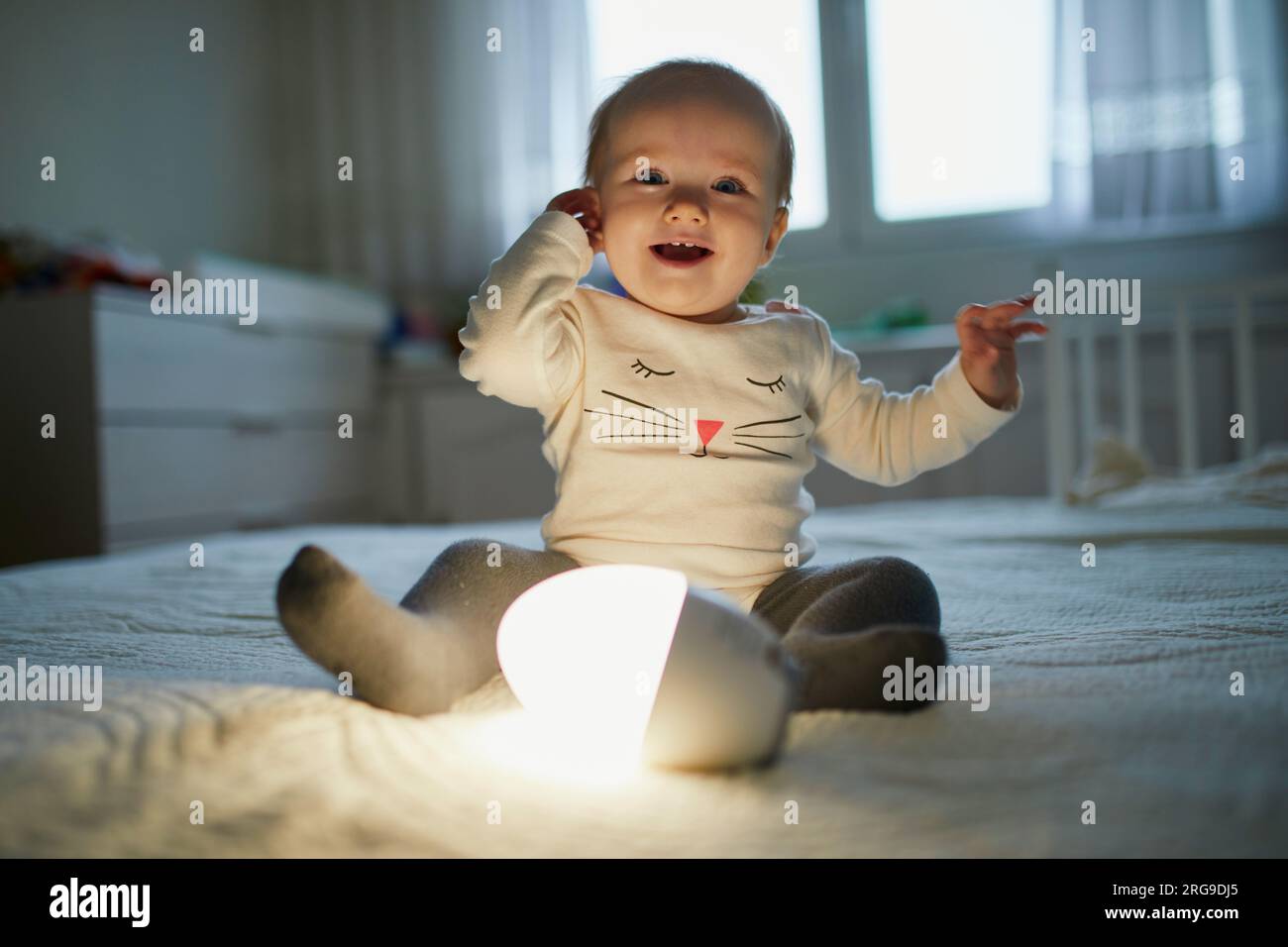 Adorable baby girl playing with bedside lamp in nursery. Happy kid ...