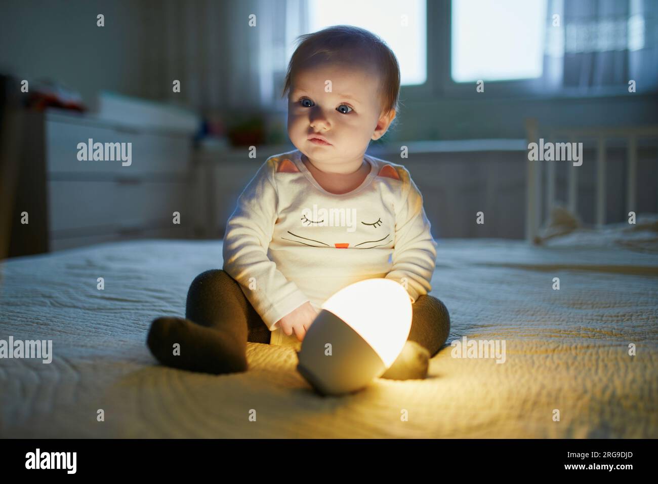 Adorable baby girl playing with bedside lamp in nursery. Happy kid ...