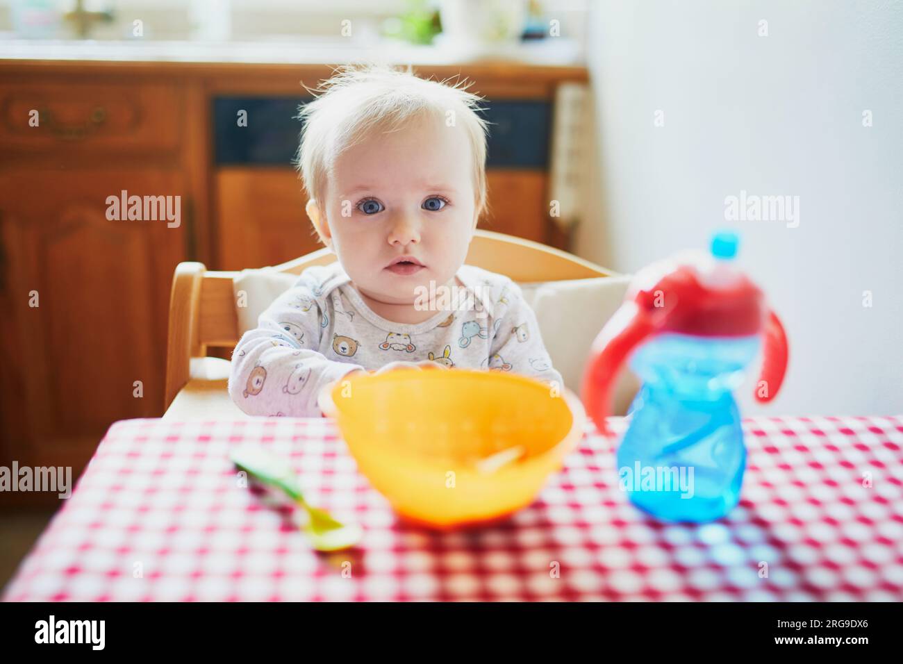Cute baby girl eating lunch in the kitchen. Little kid tasting solids ...