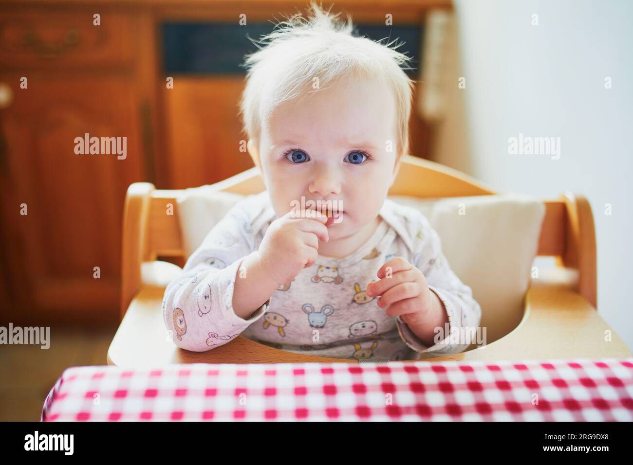 Cute baby girl feeding herself with finger food in the kitchen. Little ...