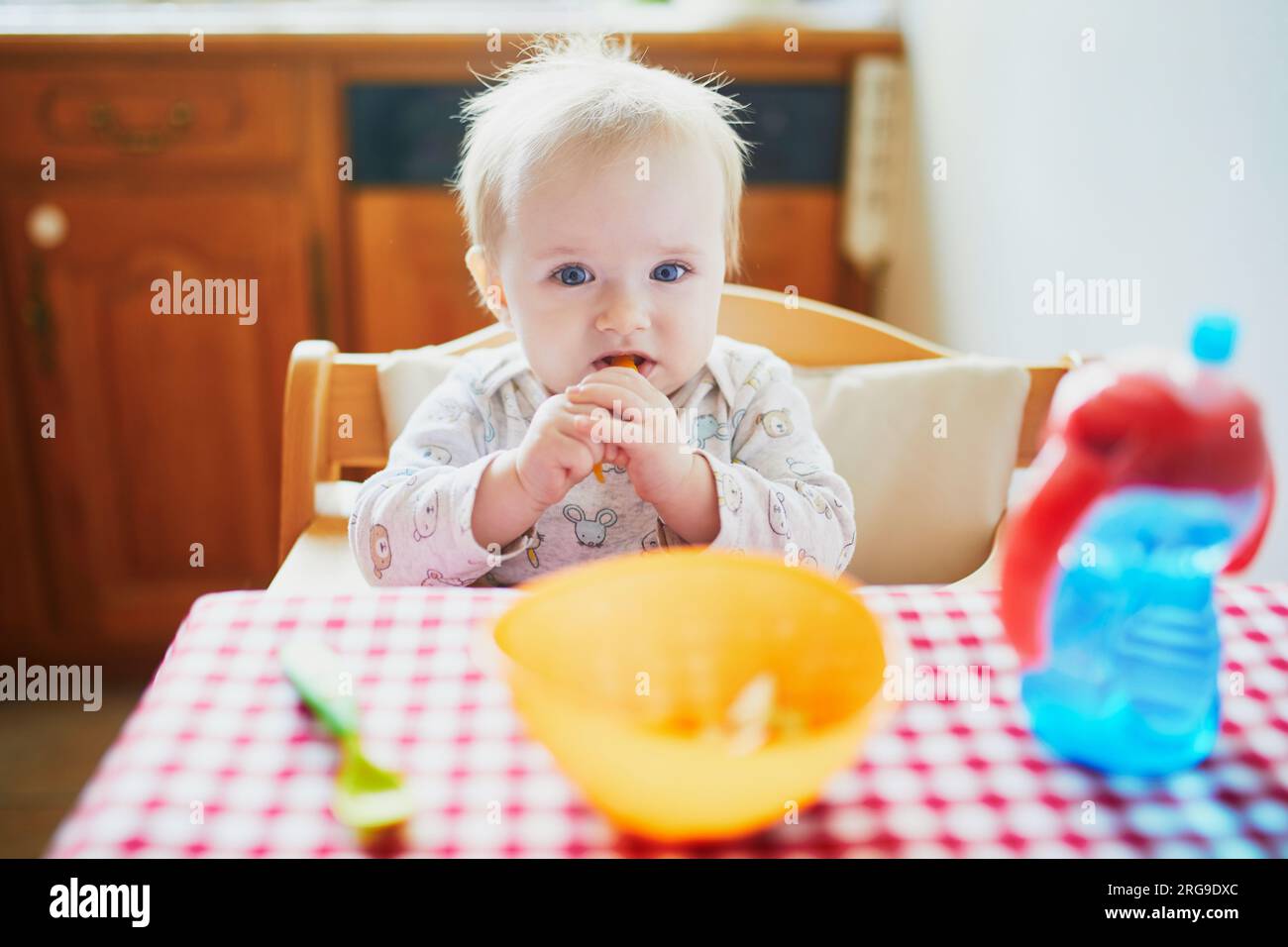 Cute baby girl feeding herself with finger food in the kitchen. Little ...