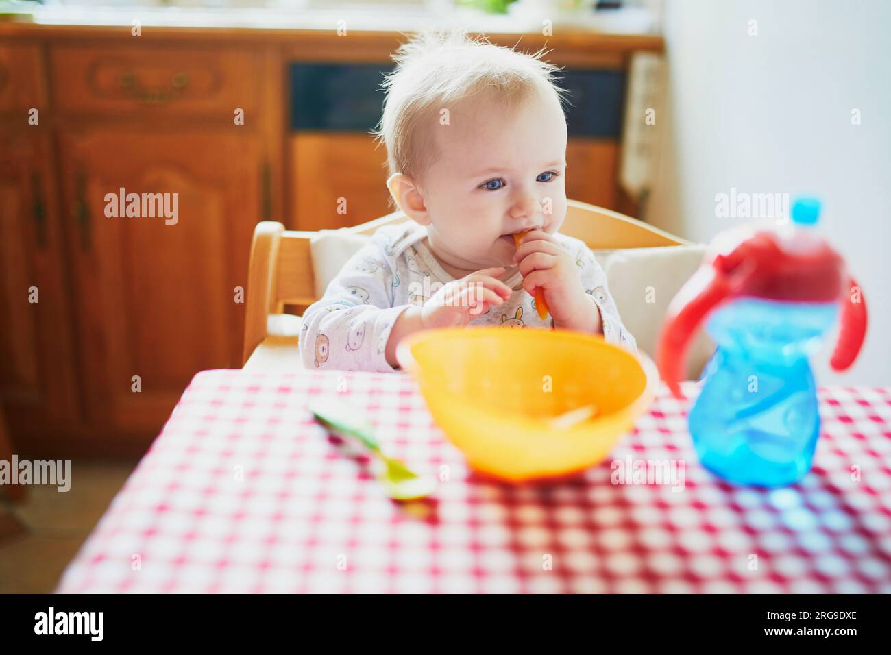 Cute baby girl eating lunch in the kitchen. Little kid tasting solids ...