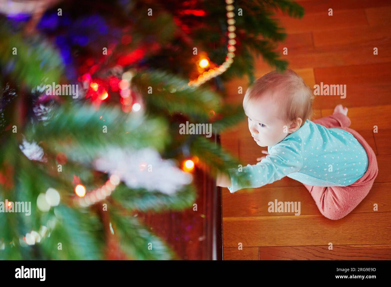 Baby girl sitting on the floor under Christmas tree. Little child ...