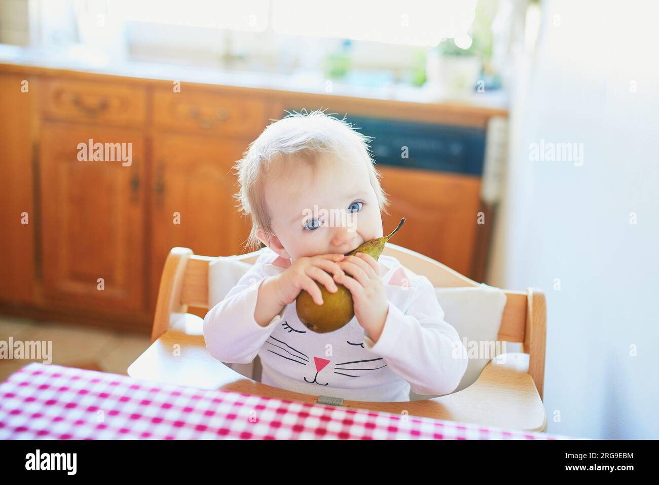 Cute baby girl eating pear in the kitchen. Little kid tasting solids at ...