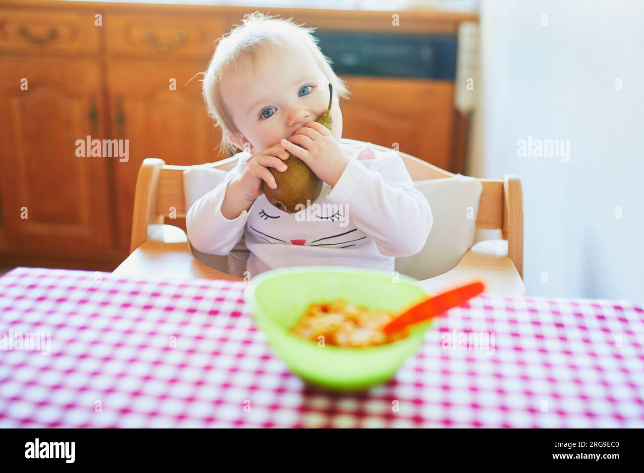 Cute baby girl eating pear in the kitchen. Little kid tasting solids at ...