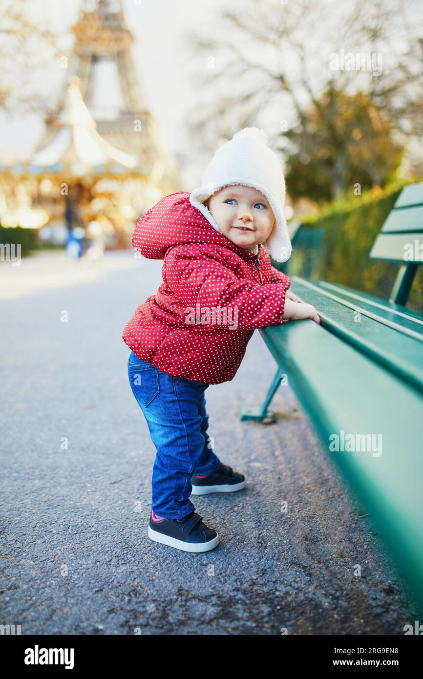 Baby girl standing on the street and holding on to bench. Little child ...