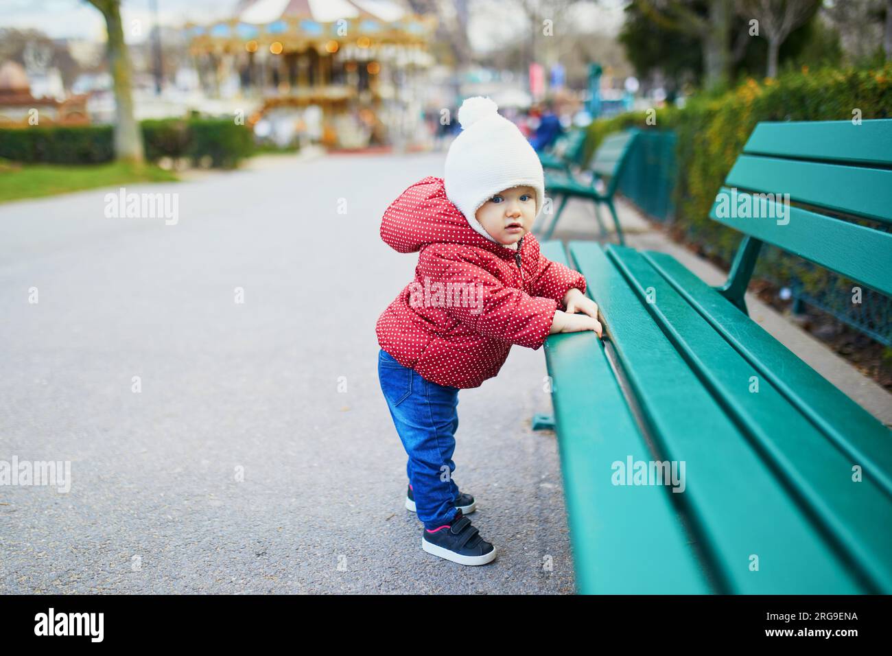 Baby girl standing on the street and holding on to bench. Little child ...