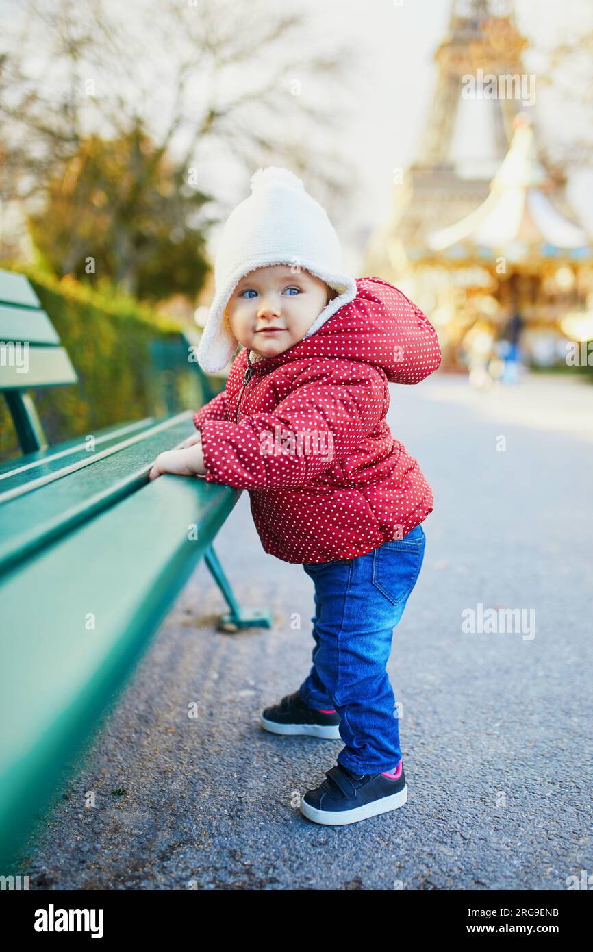 Baby girl standing on the street and holding on to bench. Little child ...