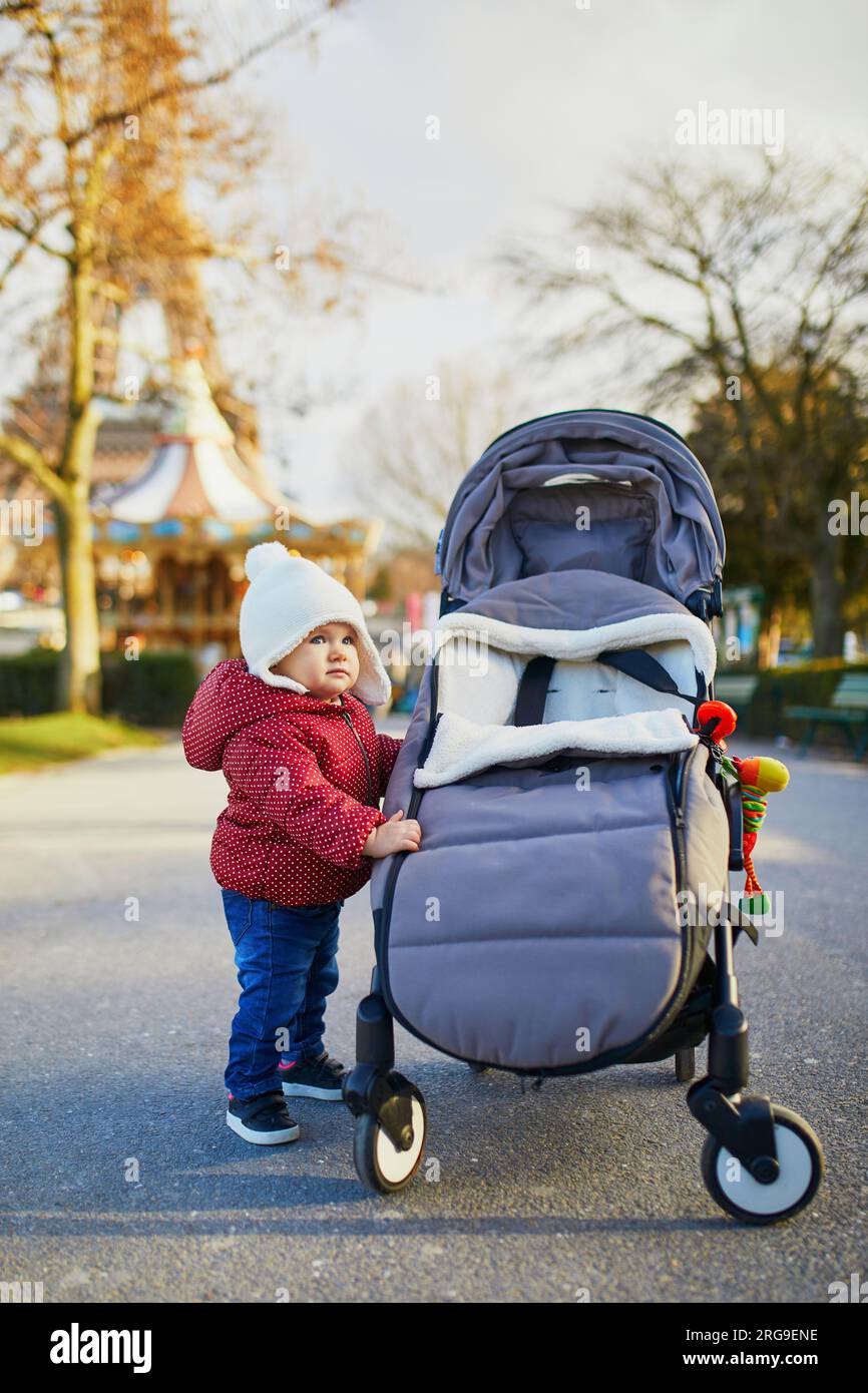 Baby girl standing on the street and holding on to pushchair. Little ...