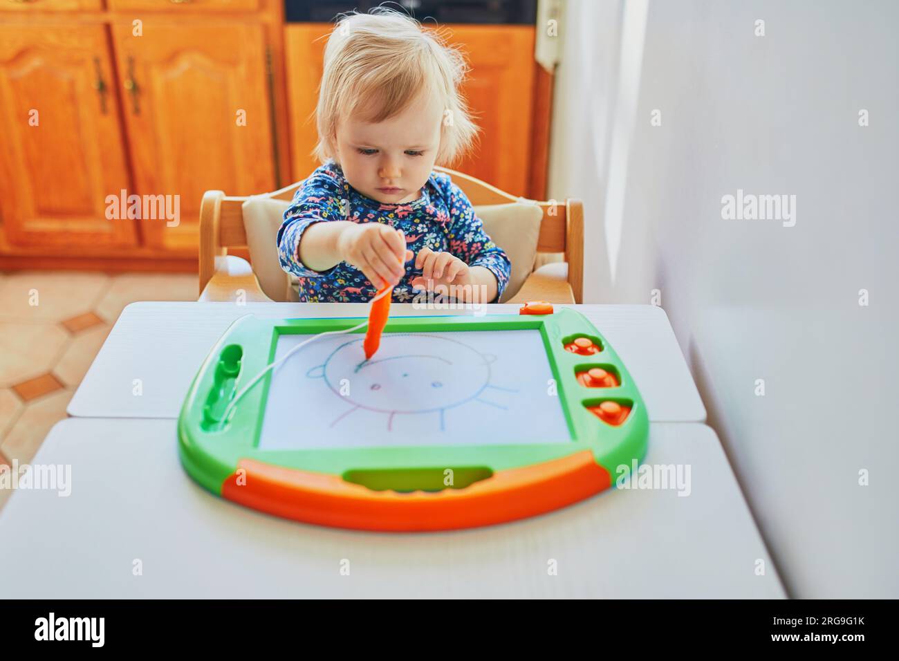 Adorable little girl drawing on magnetic magic screen at home, in ...