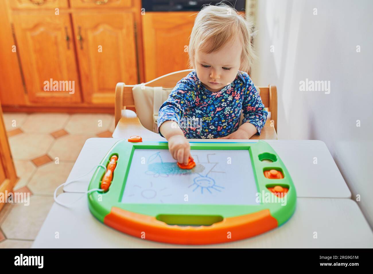 Adorable little girl drawing on magnetic magic screen at home, in ...