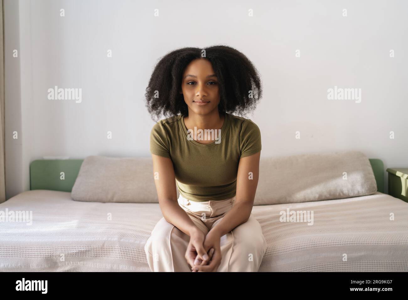 Cute African-American young black girl sits on sofa and looks at camera ...